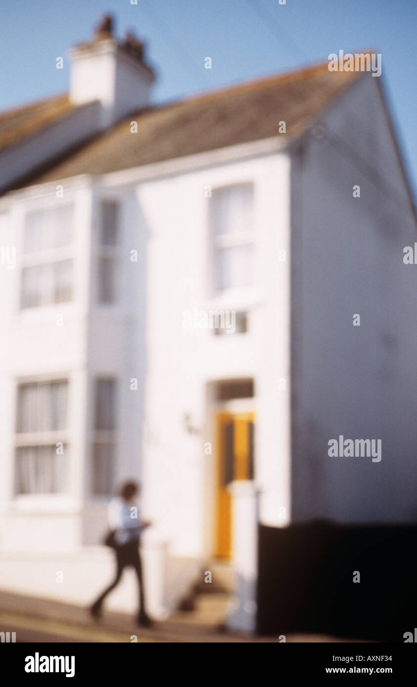 Long limbed girl or woman walking down a hill past a white house with ...