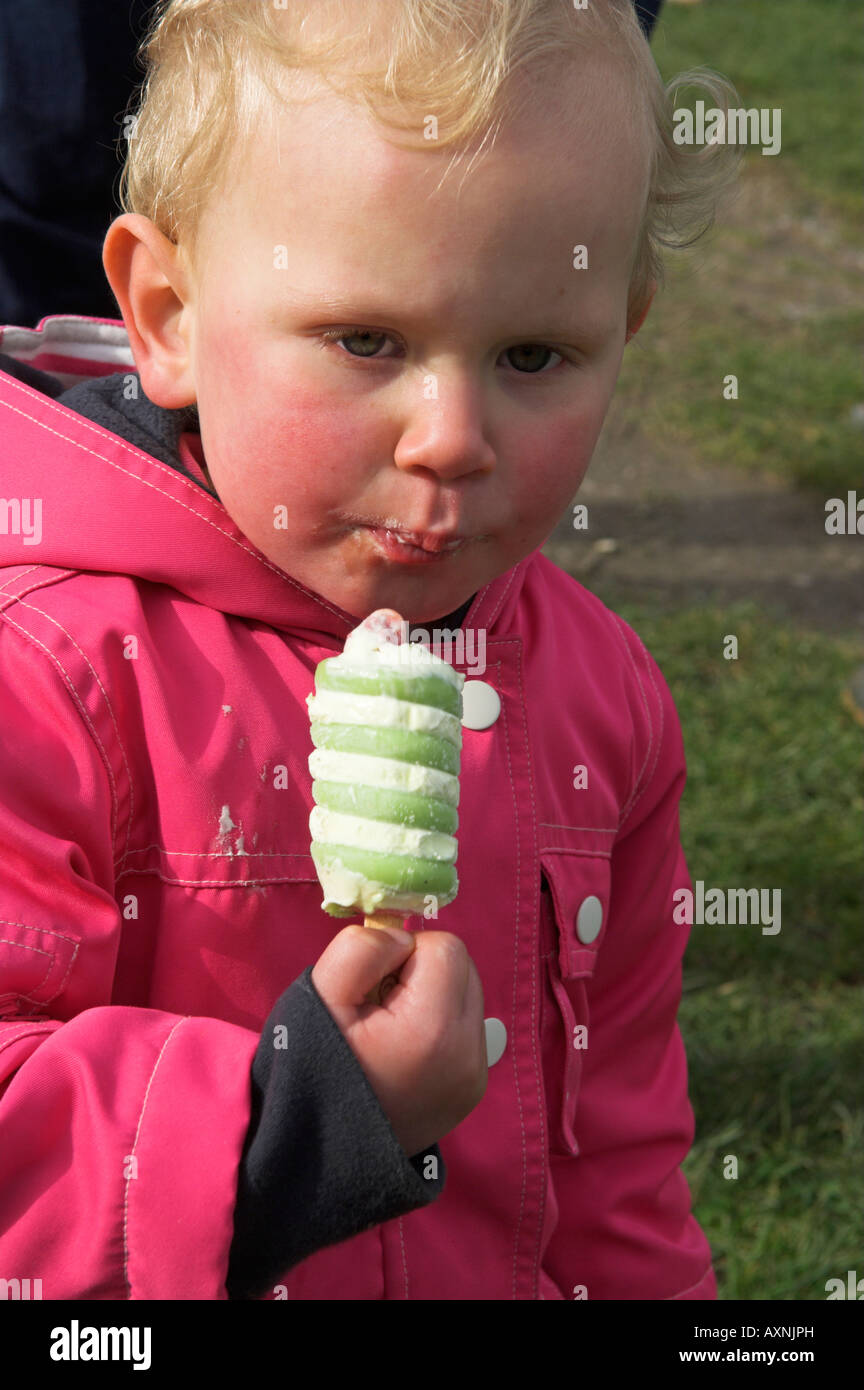 Young 4 year old girl in pink coat eating "ice cream" during winter ...