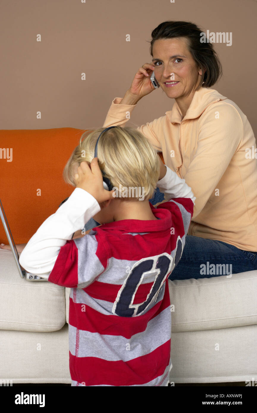 Mother phoning with a mobile phone on a sofa, son (4-5 Years) listening ...