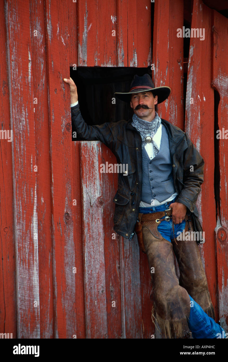 Cowboy leaning against weathered red barn Stock Photo - Alamy