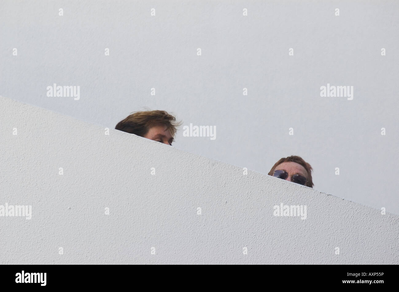 2 faces looking over a white wall Stock Photo - Alamy