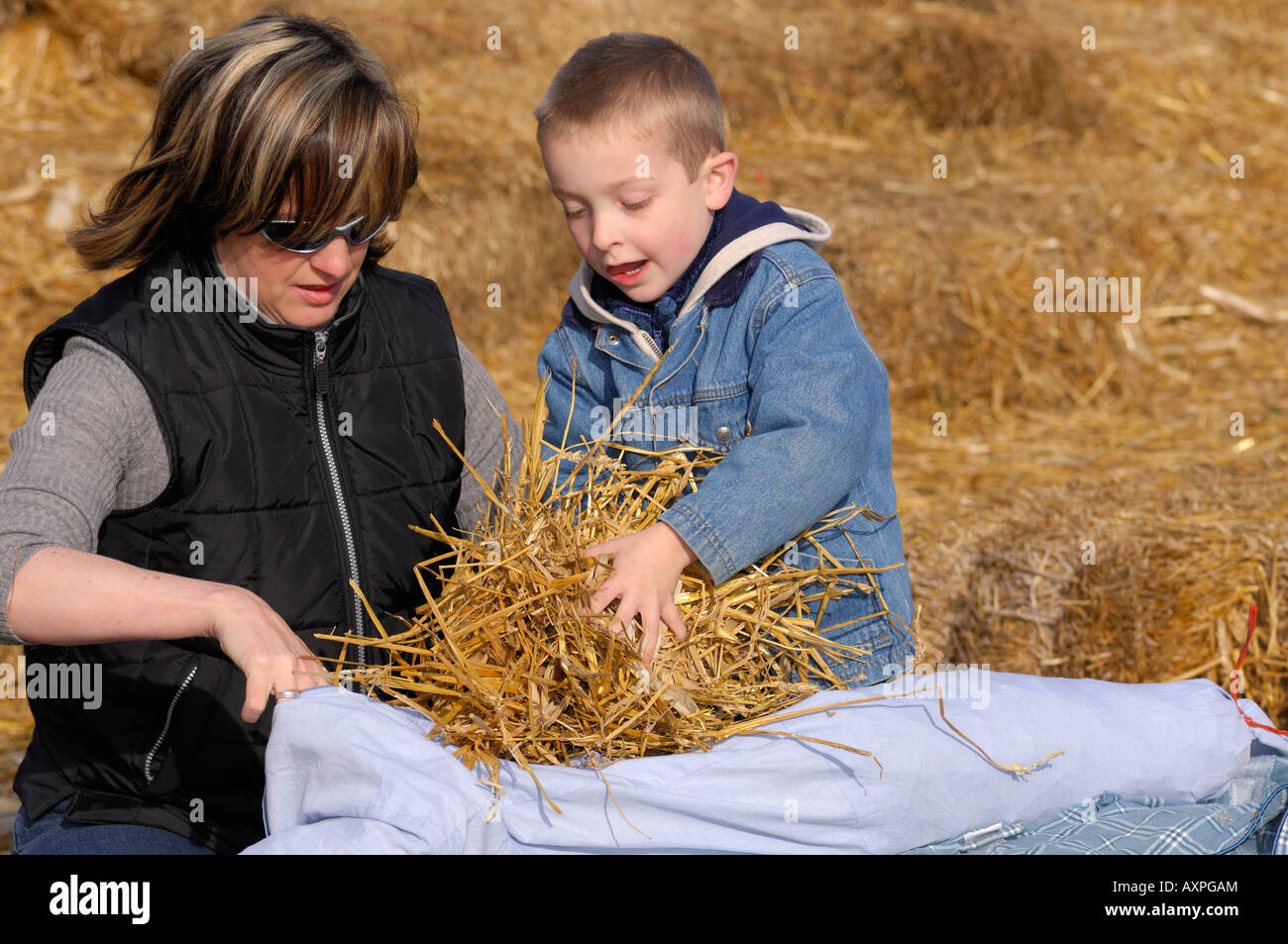 Mother and son making a scarecrow by stuffing straw into old clothing ...