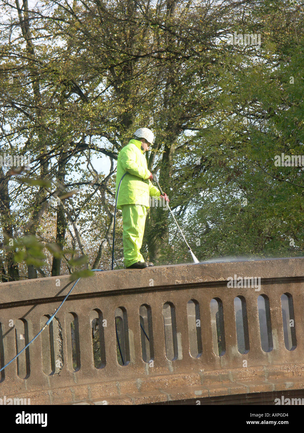 A workman cleans an old precast concrete bridge with a high pressure ...