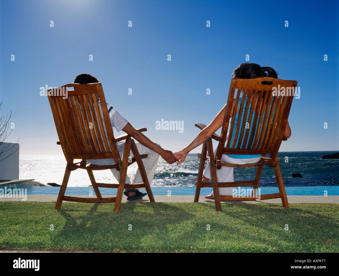 Rear view of a young couple sitting on chairs holding hands Stock Photo ...