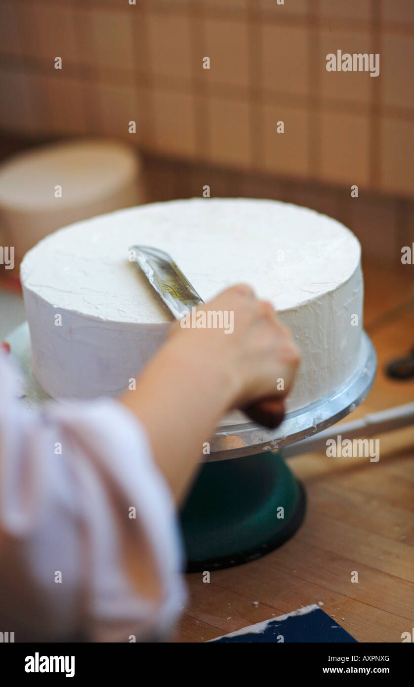 Pastry chef spreading icing over top of white cream cake Stock Photo ...
