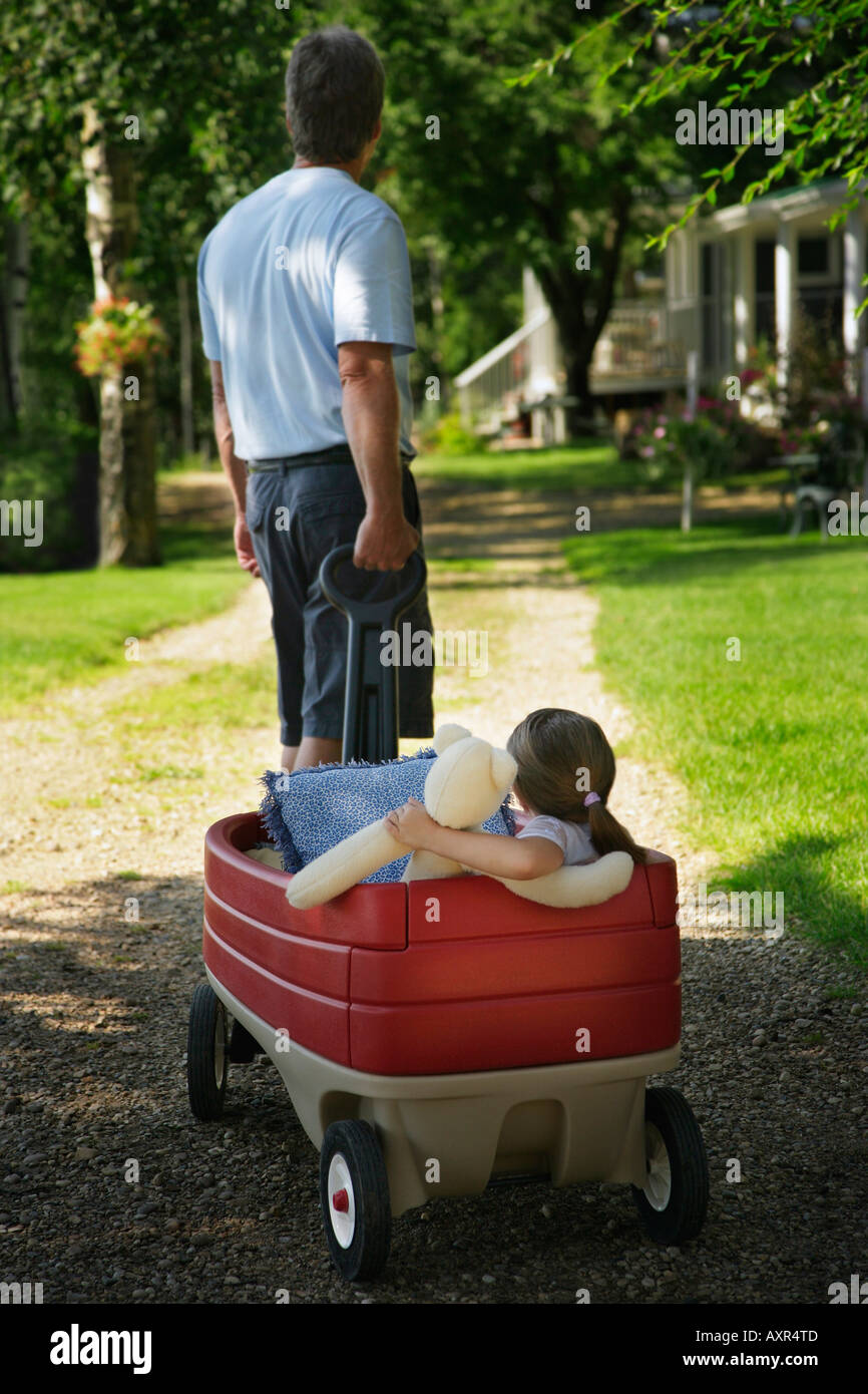 Man pulling girl in red wagon Stock Photo - Alamy