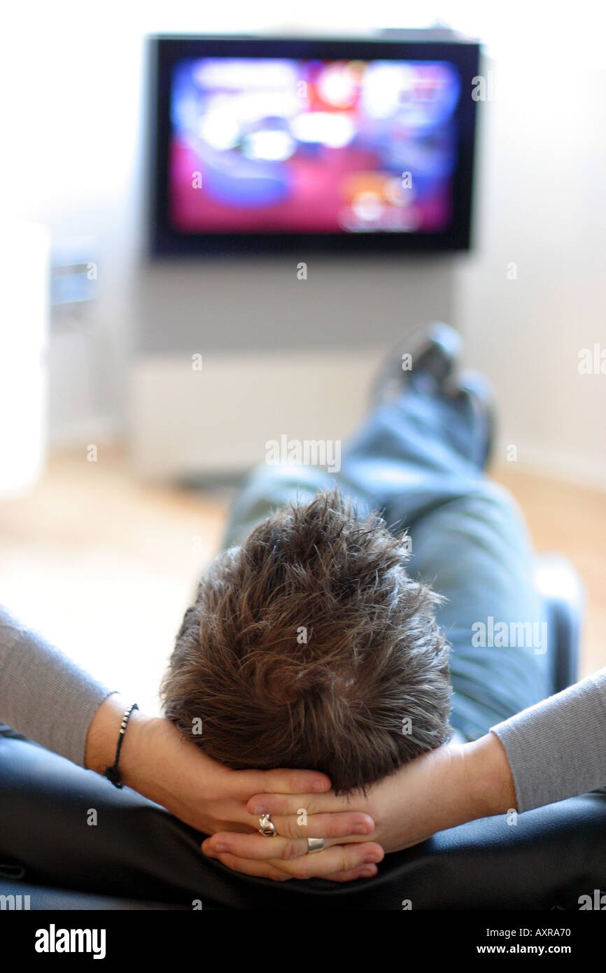 Man watching television TV in a loft apartment Stock Photo - Alamy