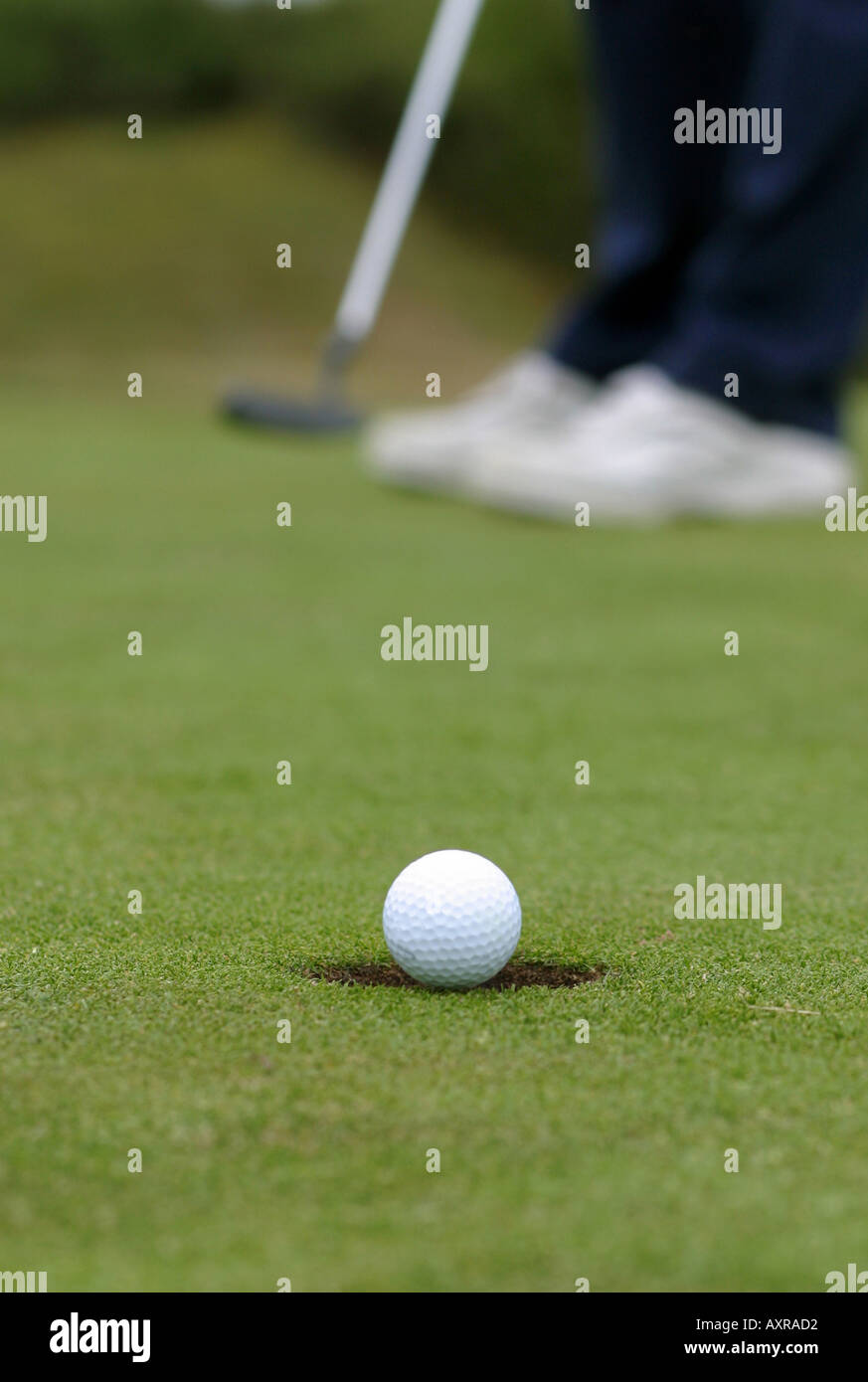 A golf ball about to fall down a hole on a green Stock Photo - Alamy