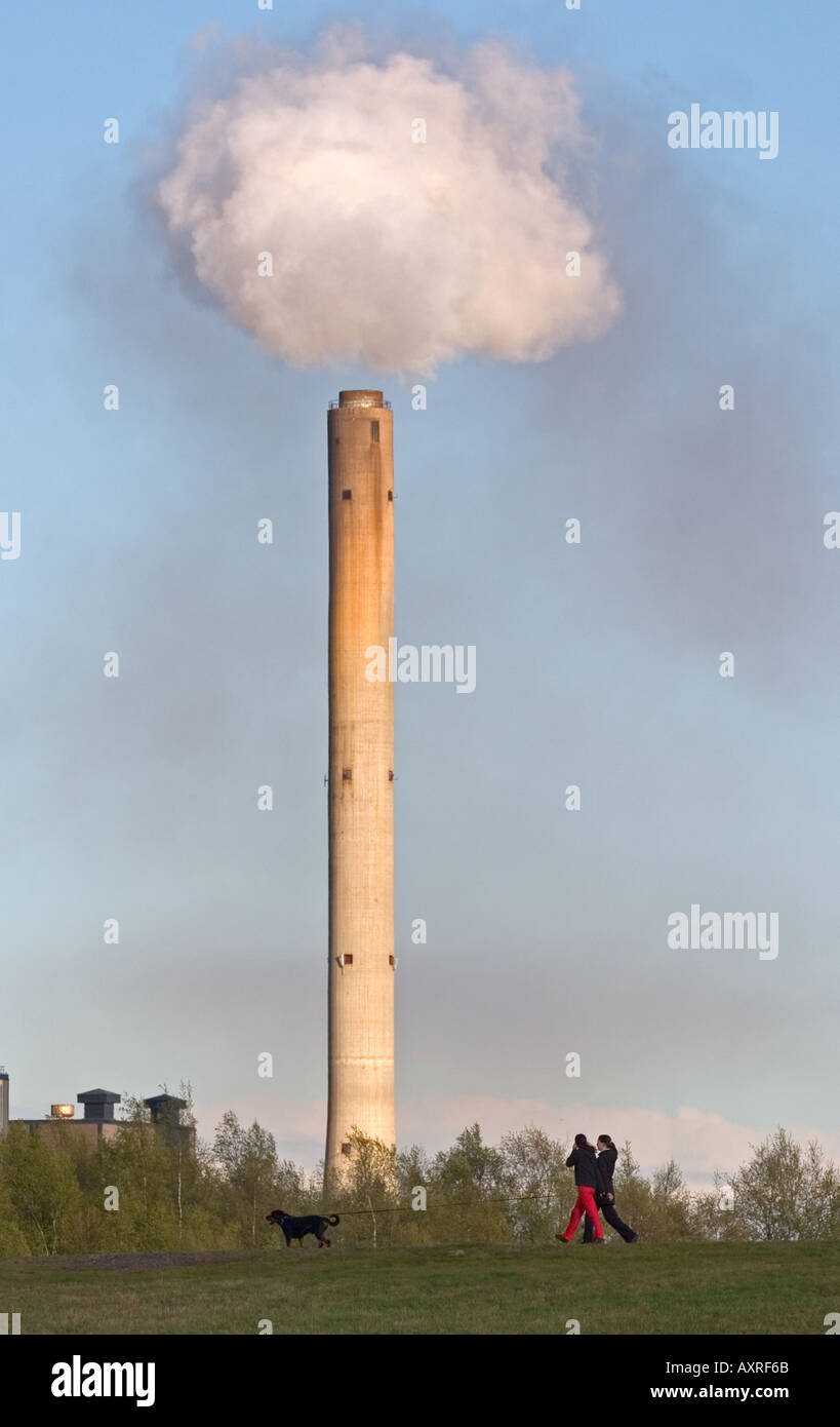 Peat burning power plant polluting the air. Two young women walking a ...
