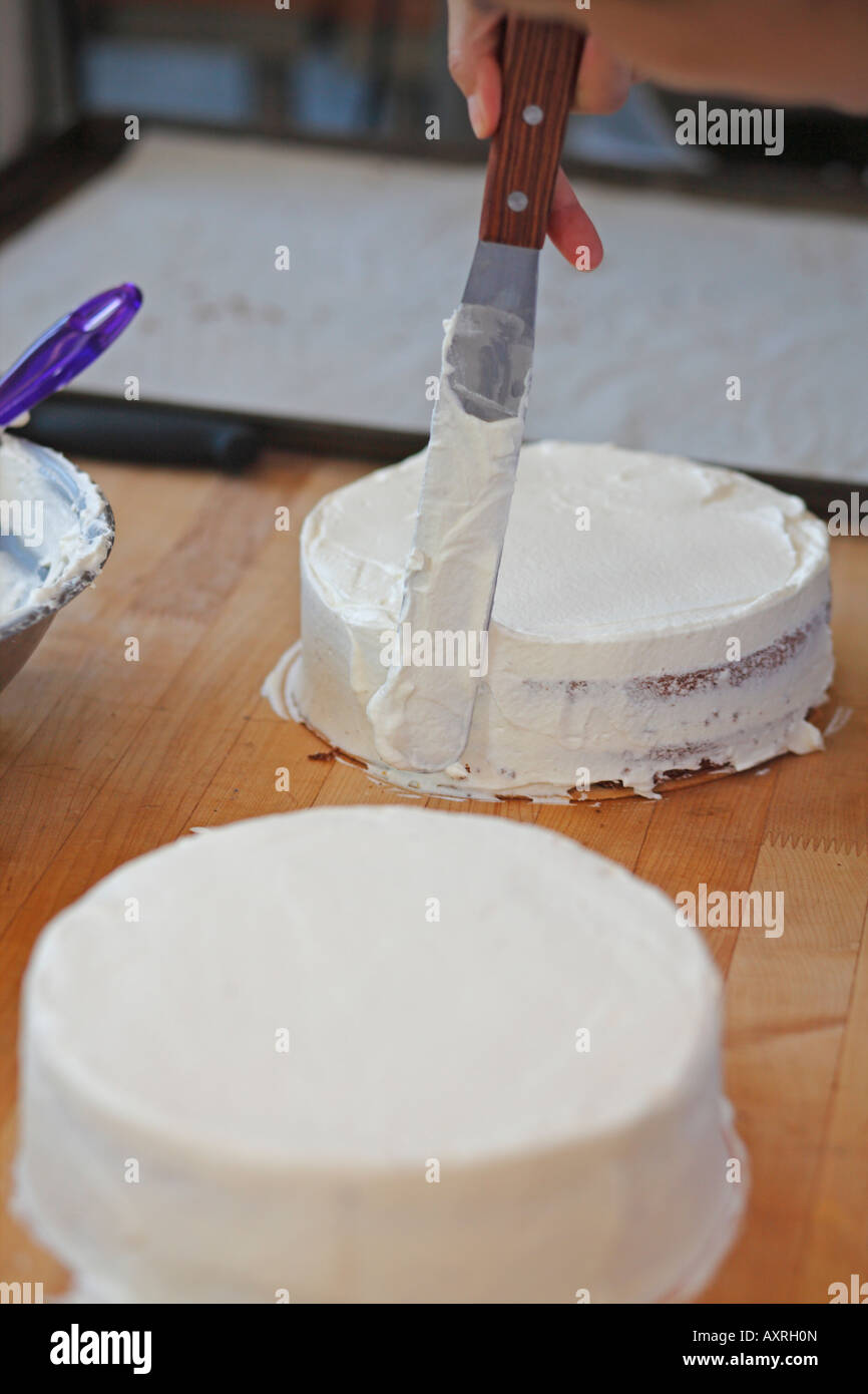Pastry chef spreading icing over white cream sponge cakes Stock Photo ...
