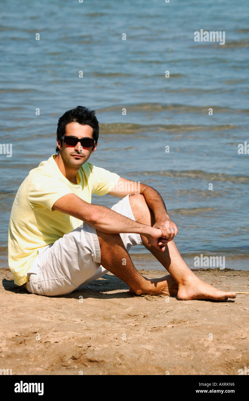 Young man sitting on beach Stock Photo - Alamy