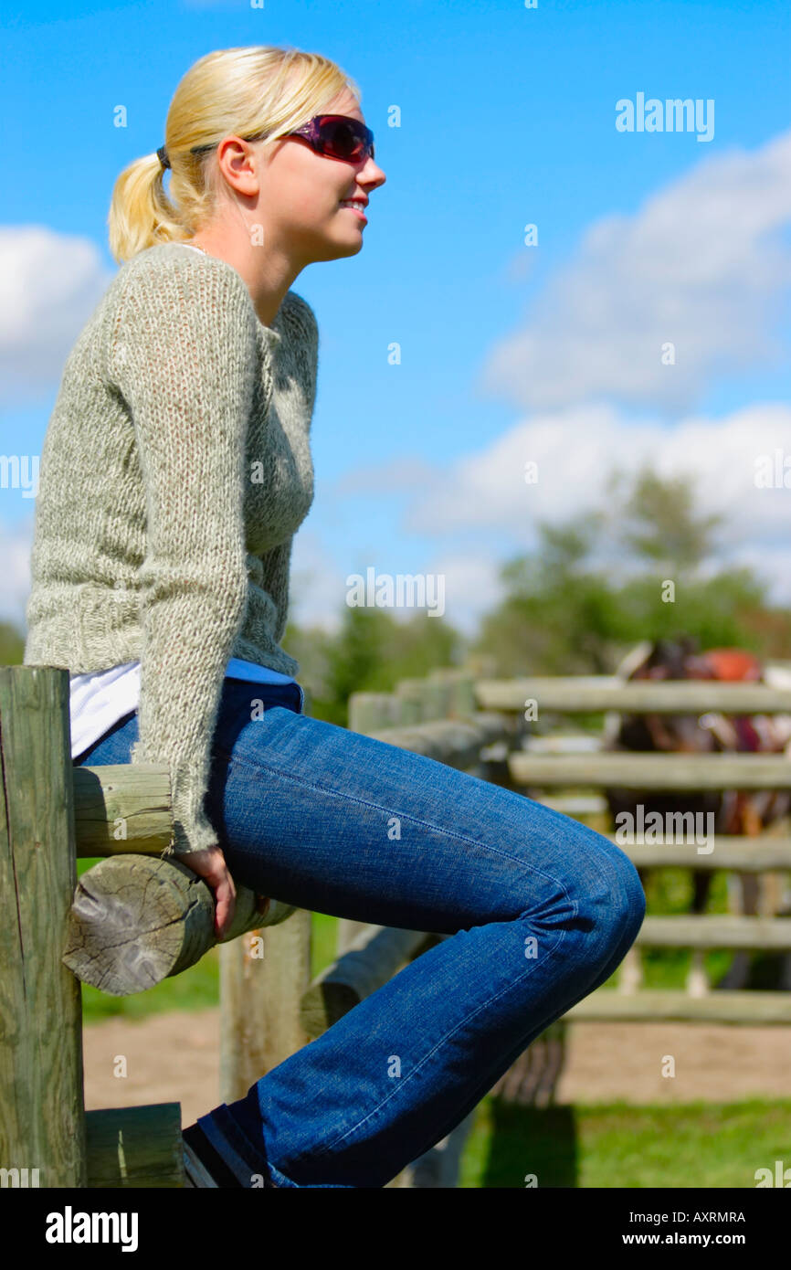 Young woman sitting on corral railing Stock Photo - Alamy