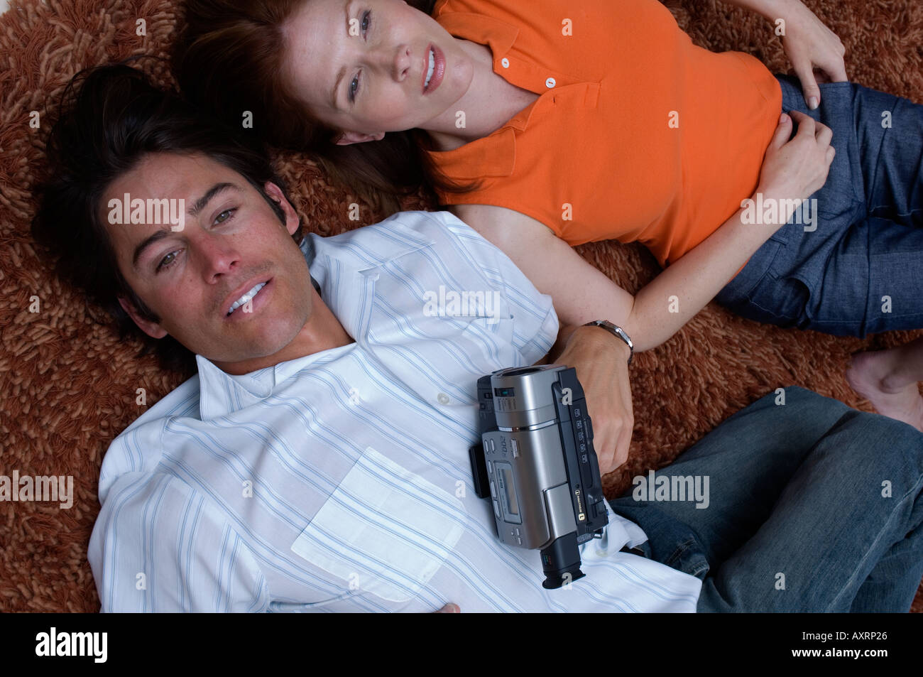 Portrait of couple looking at their video camera while laying on the ...
