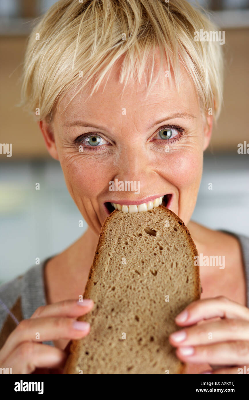 Mature woman with blond hair biting into a slice of bread, close-up ...