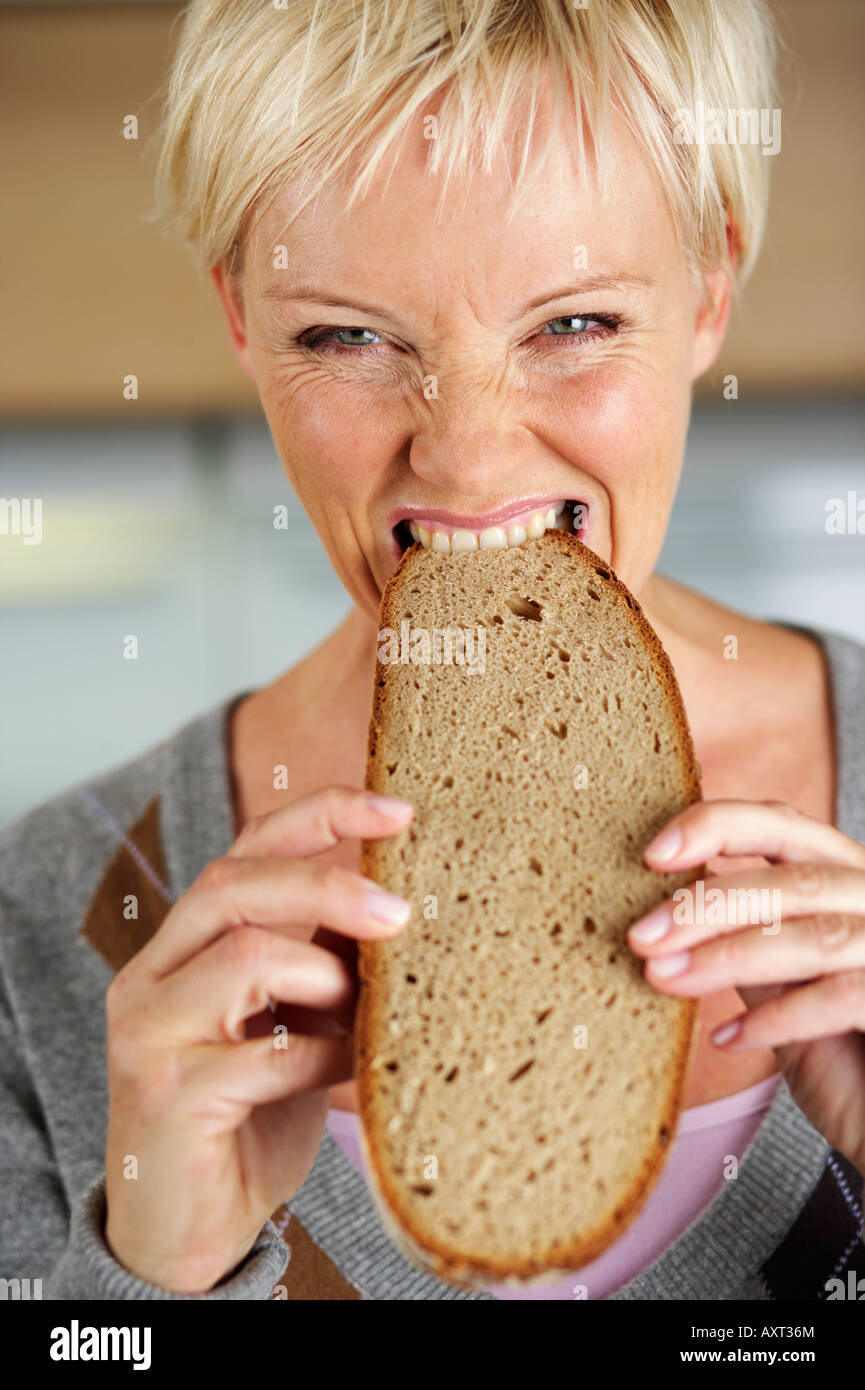 Mature woman with blond hair biting into a slice of bread, close-up ...