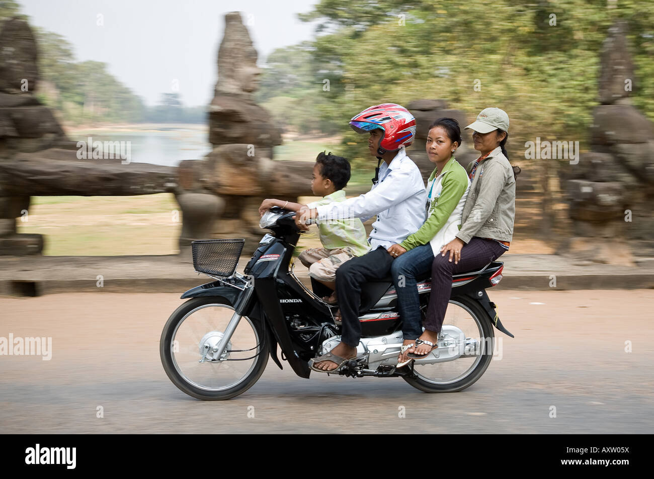 A family of 4 rides by on a single motorcycle outside of the temples in ...