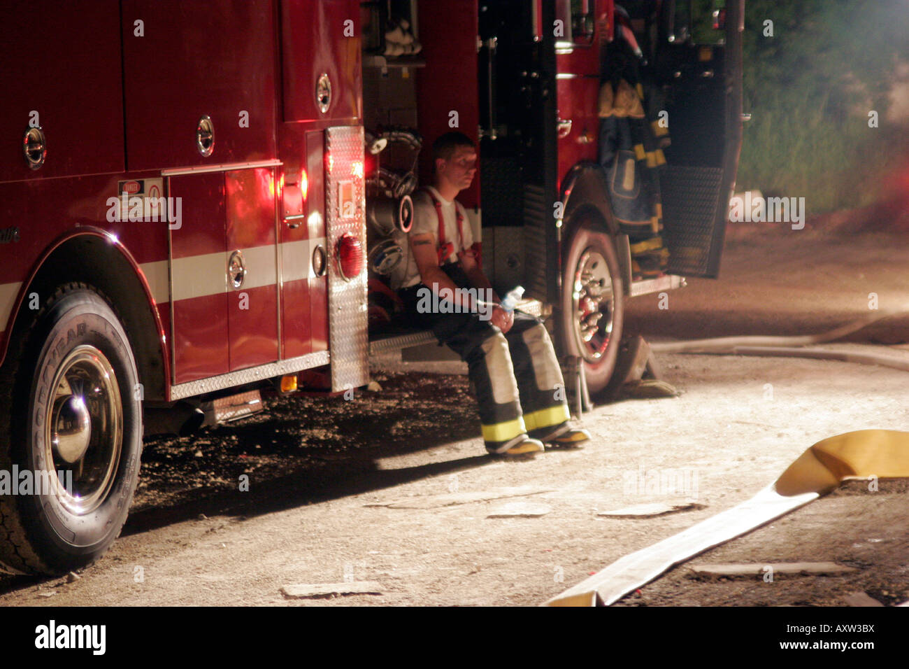 A firefighter sitting and resting on the step of the fire engine with a ...