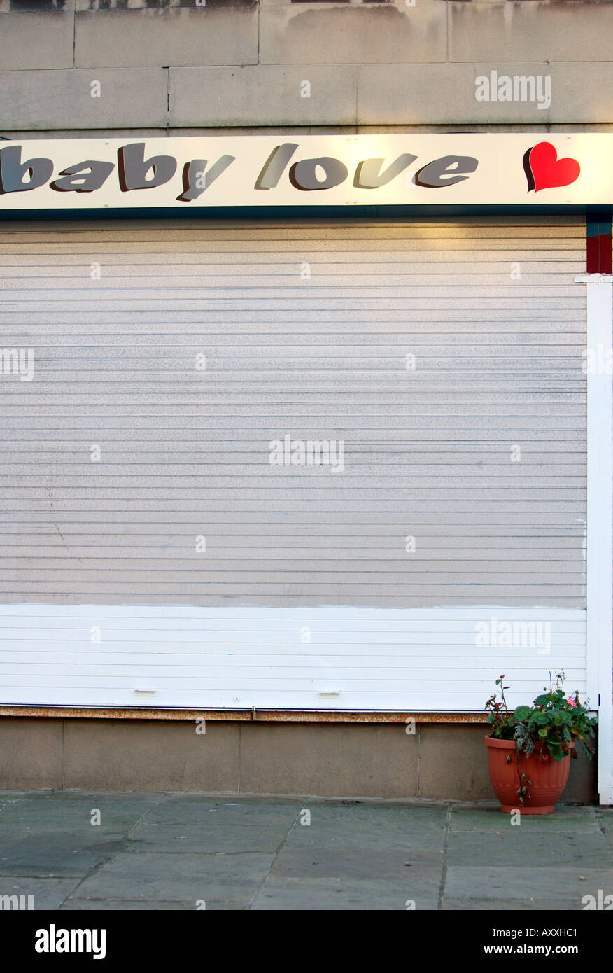 Shop front closed with shutters down with a small plant pot in the ...