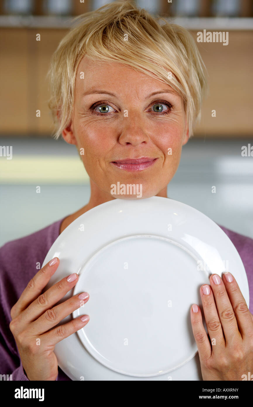 Blond woman peering over the rim of a plate, close-up Stock Photo - Alamy