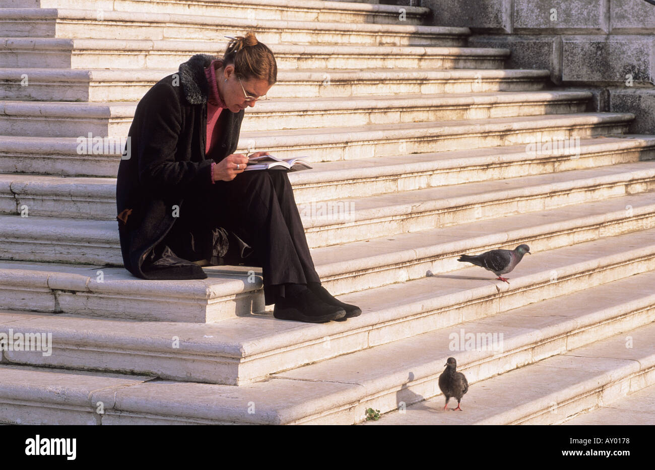 woman dressed in a dark coat reading a guide book on the steps of the ...
