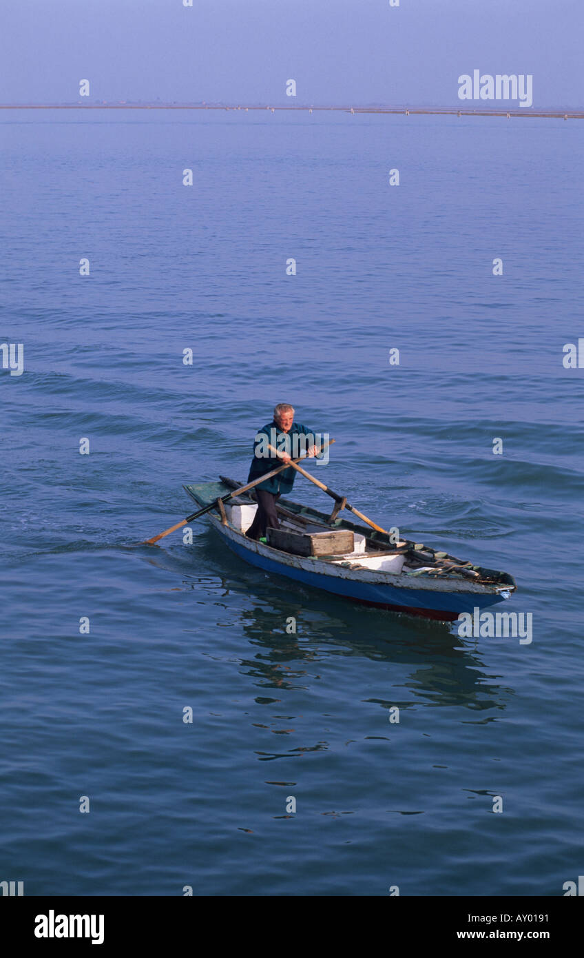 A man rowing a fishing boat in a standing postion surounded by blue ...
