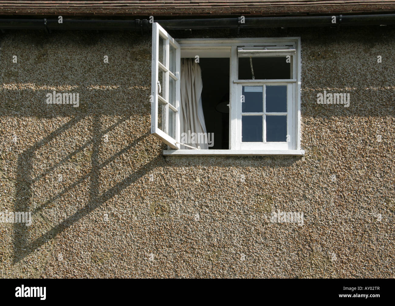Open window of a house casting a strong geometric shadow across pebble ...