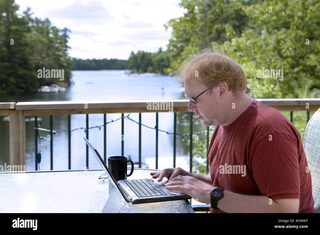 Man working on a computer on his lake side deck Stock Photo - Alamy