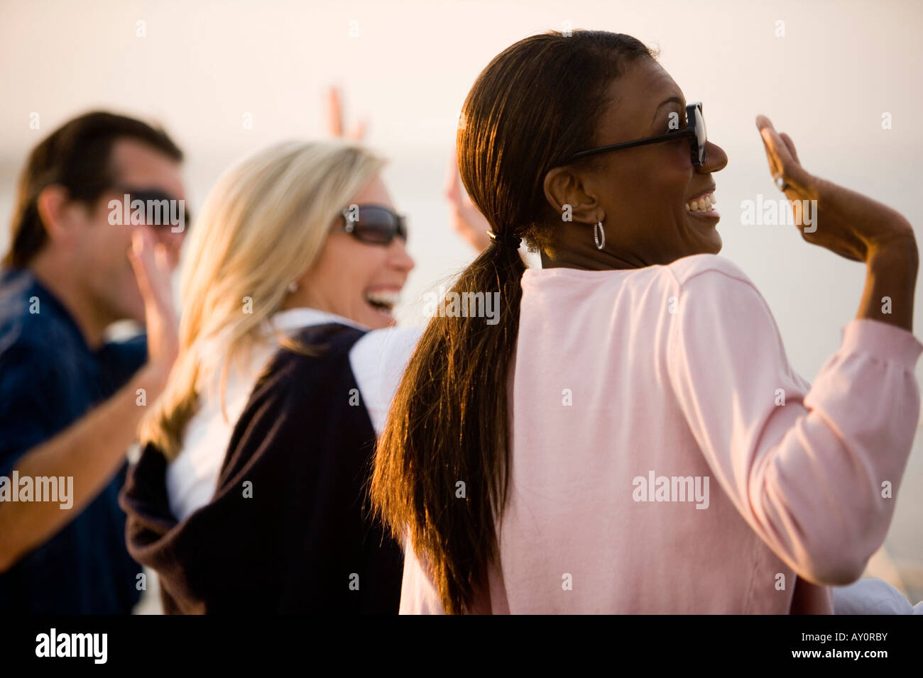 Cheerful friends waving while looking away Stock Photo - Alamy
