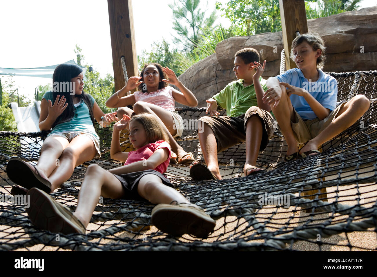 Teenagers sitting on net tied to wooden columns Stock Photo - Alamy
