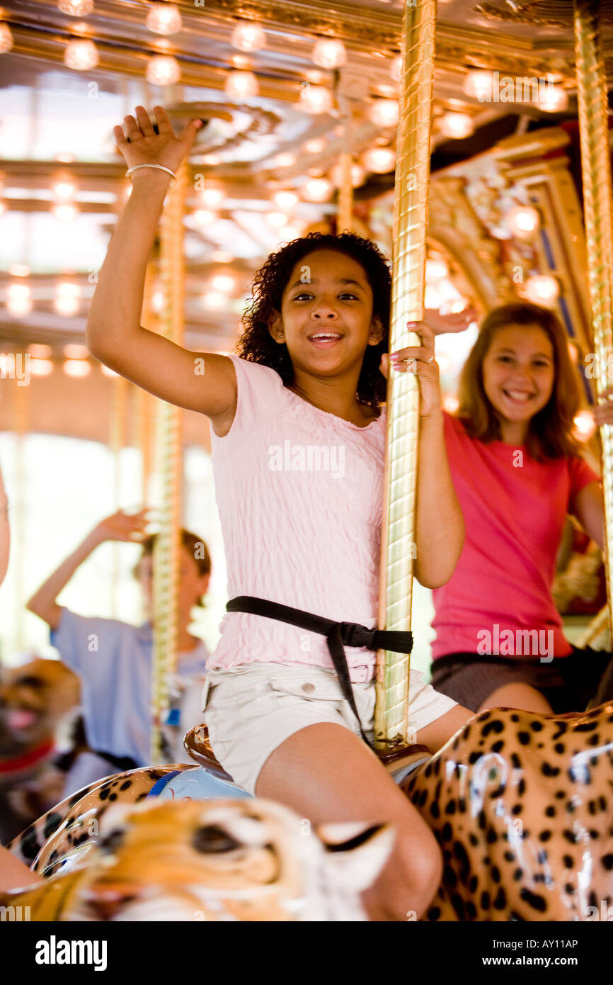 Portrait of cheerful teenage girls sitting on a carousel and waving ...