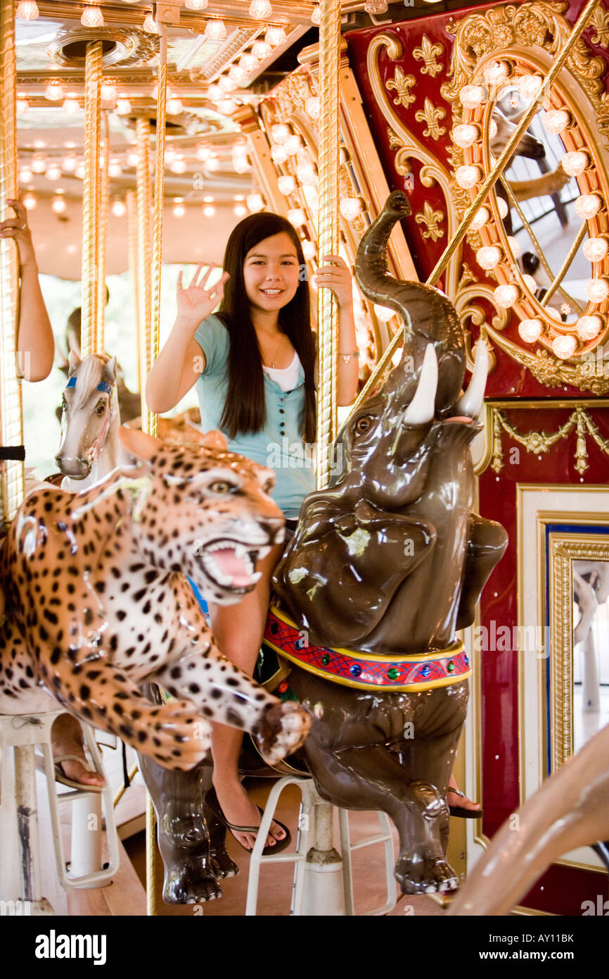 Portrait of a cheerful teenage girl sitting on a carousel and waving ...