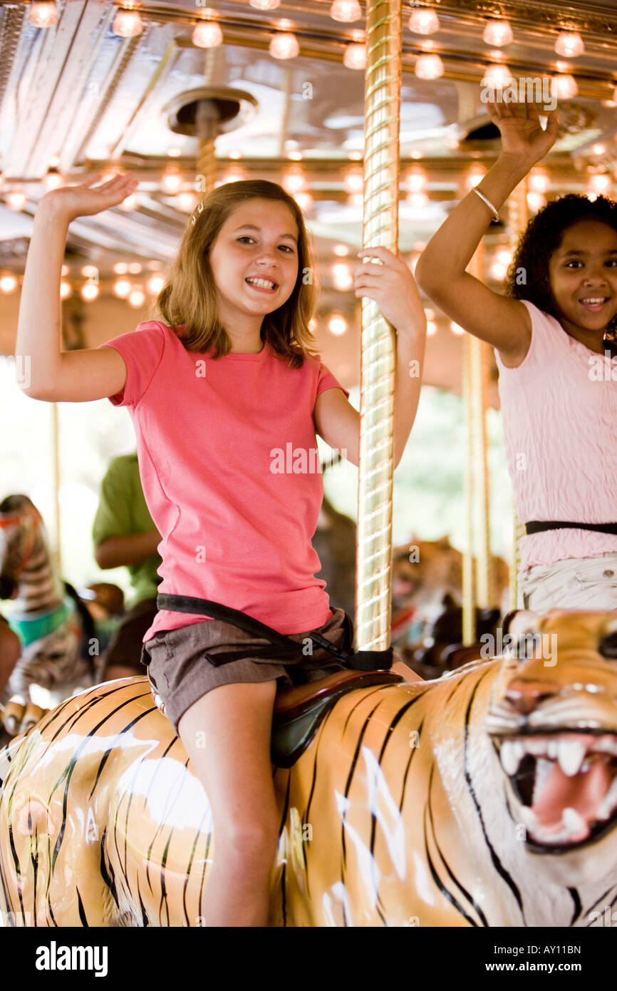 Portrait of cheerful teenage girls sitting on a carousel and waving ...