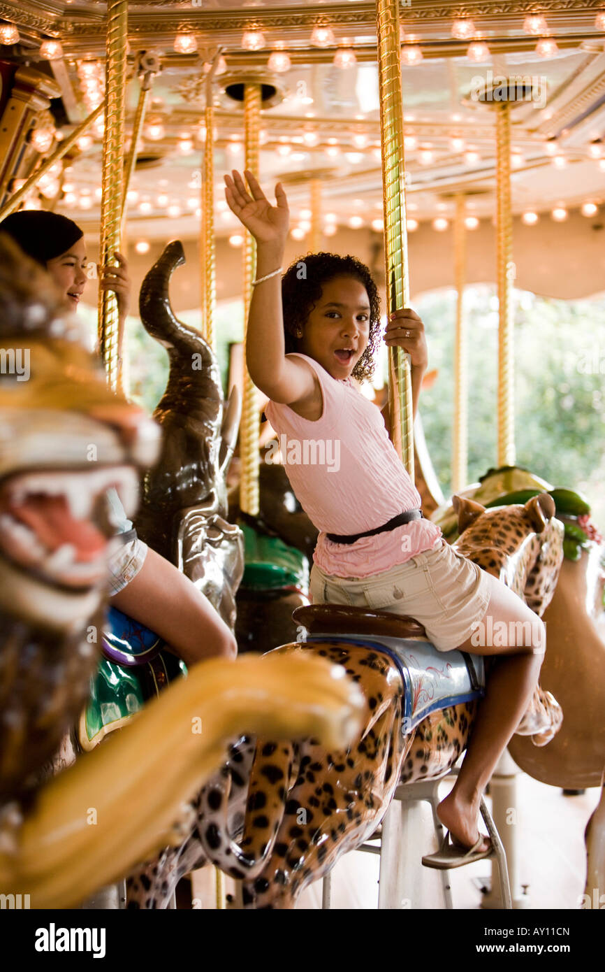 Portrait of a cheerful teenage girls sitting on a carousel and waving ...