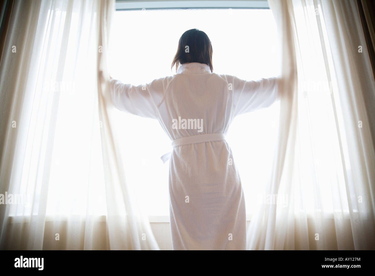 Young woman opening curtain Stock Photo - Alamy