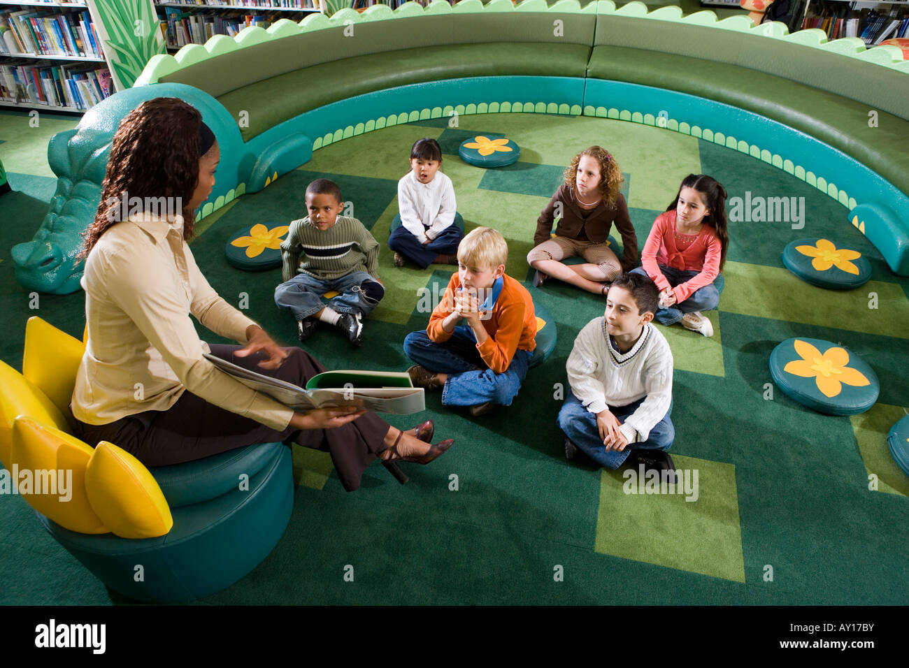 Teacher showing book to students sitting on floor in the library Stock ...