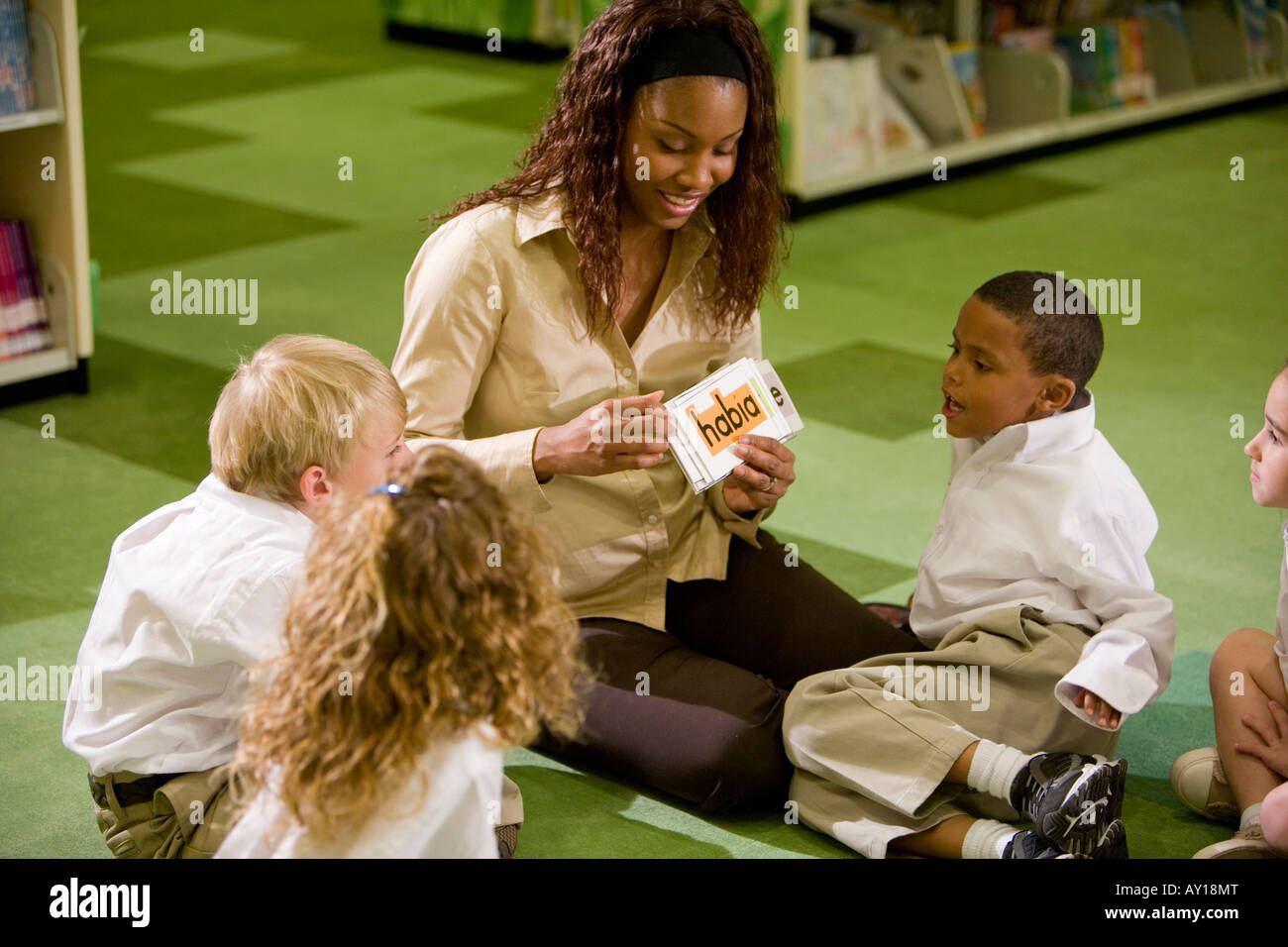 Teacher showing flash cards to students sitting on floor in the library ...
