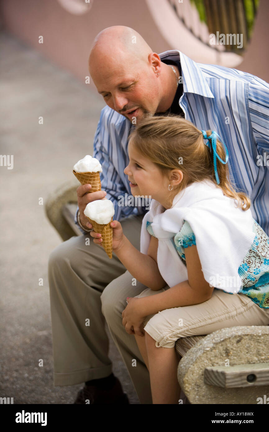 Father and daughter sitting on a bench and holding ice cream cones ...