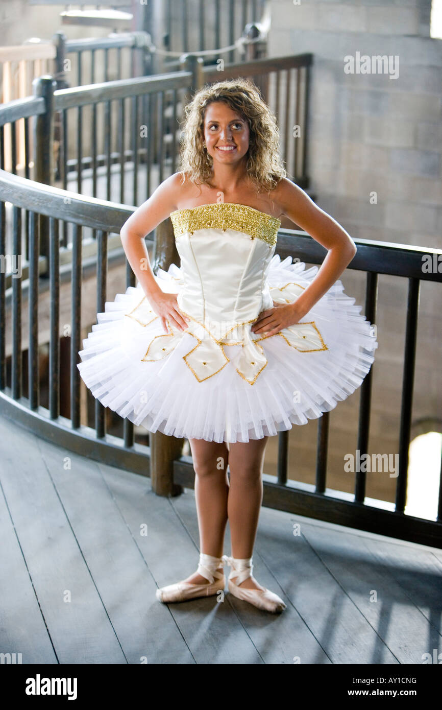 Cheerful ballet dancer standing by wooden railing with hand on hip ...