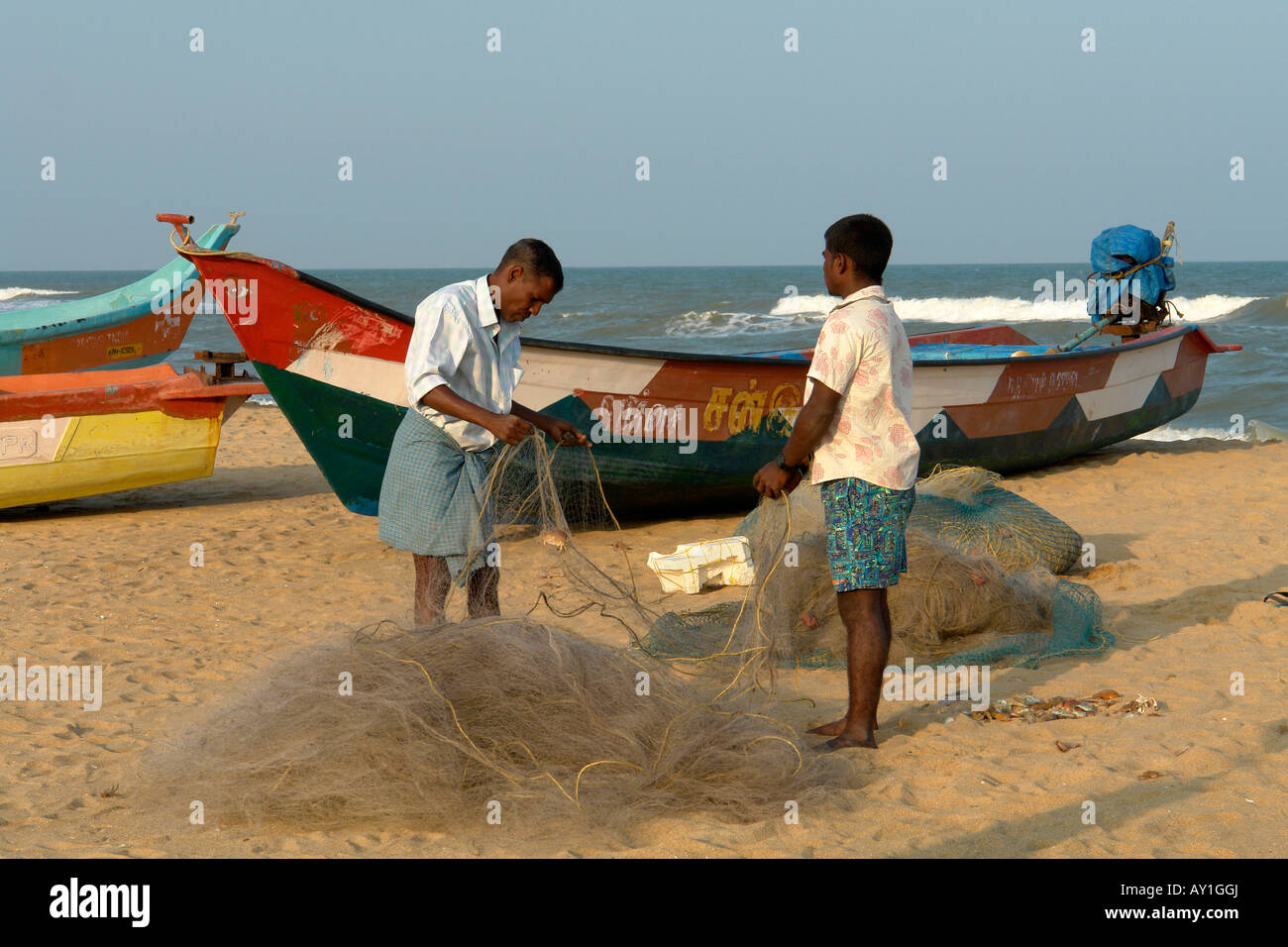 two indian fishermen checking their nets with traditional fishing boats ...