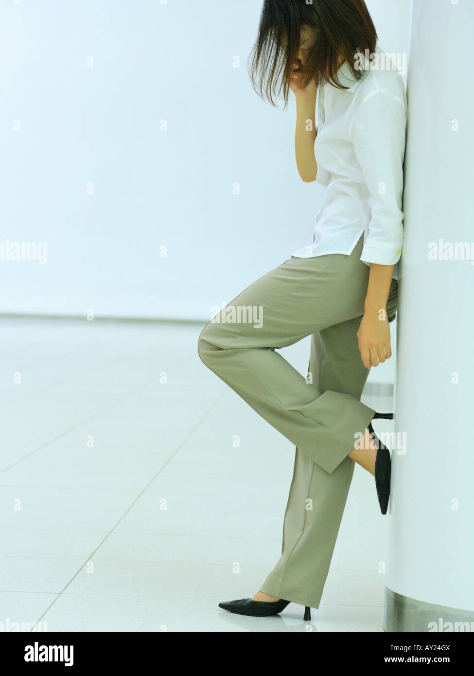 Side profile of a woman leaning against a wall and talking on a mobile ...