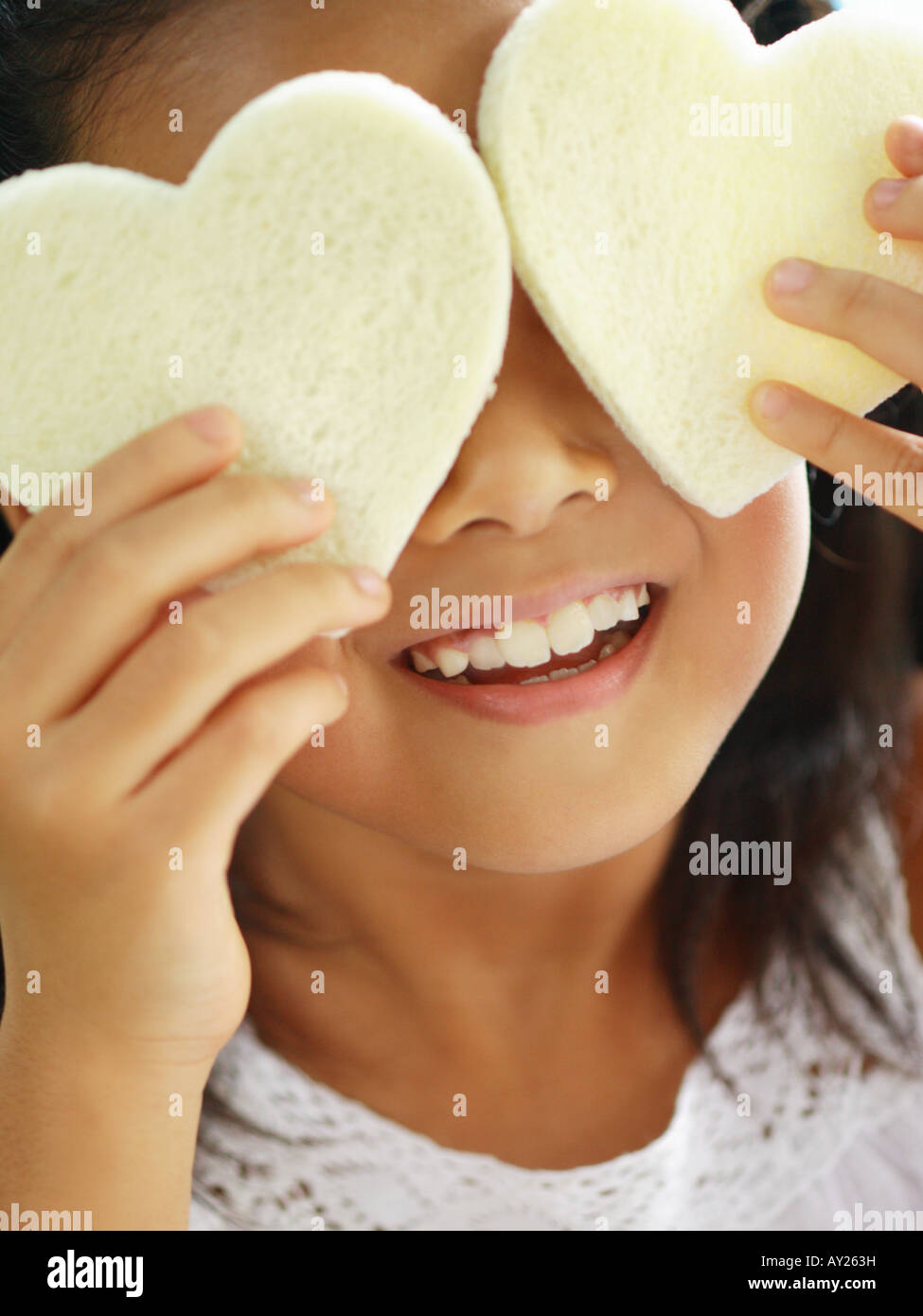 Close-up of a girl holding two heart shaped breads in front of her eyes ...