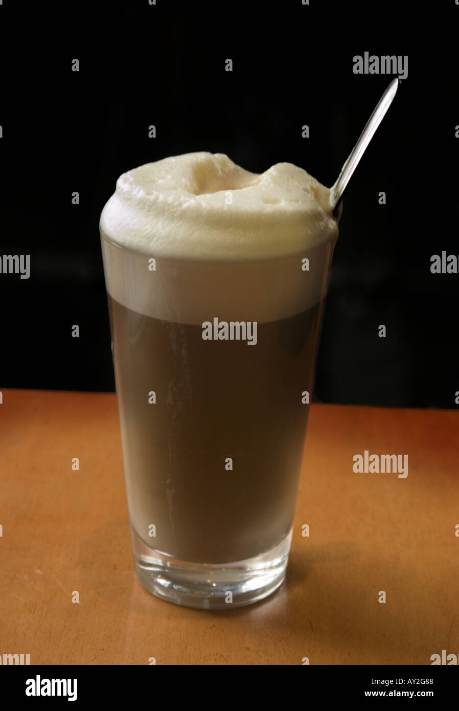 Cafe Latte' in a tall glass with lots of foam and froth with a spoon on ...