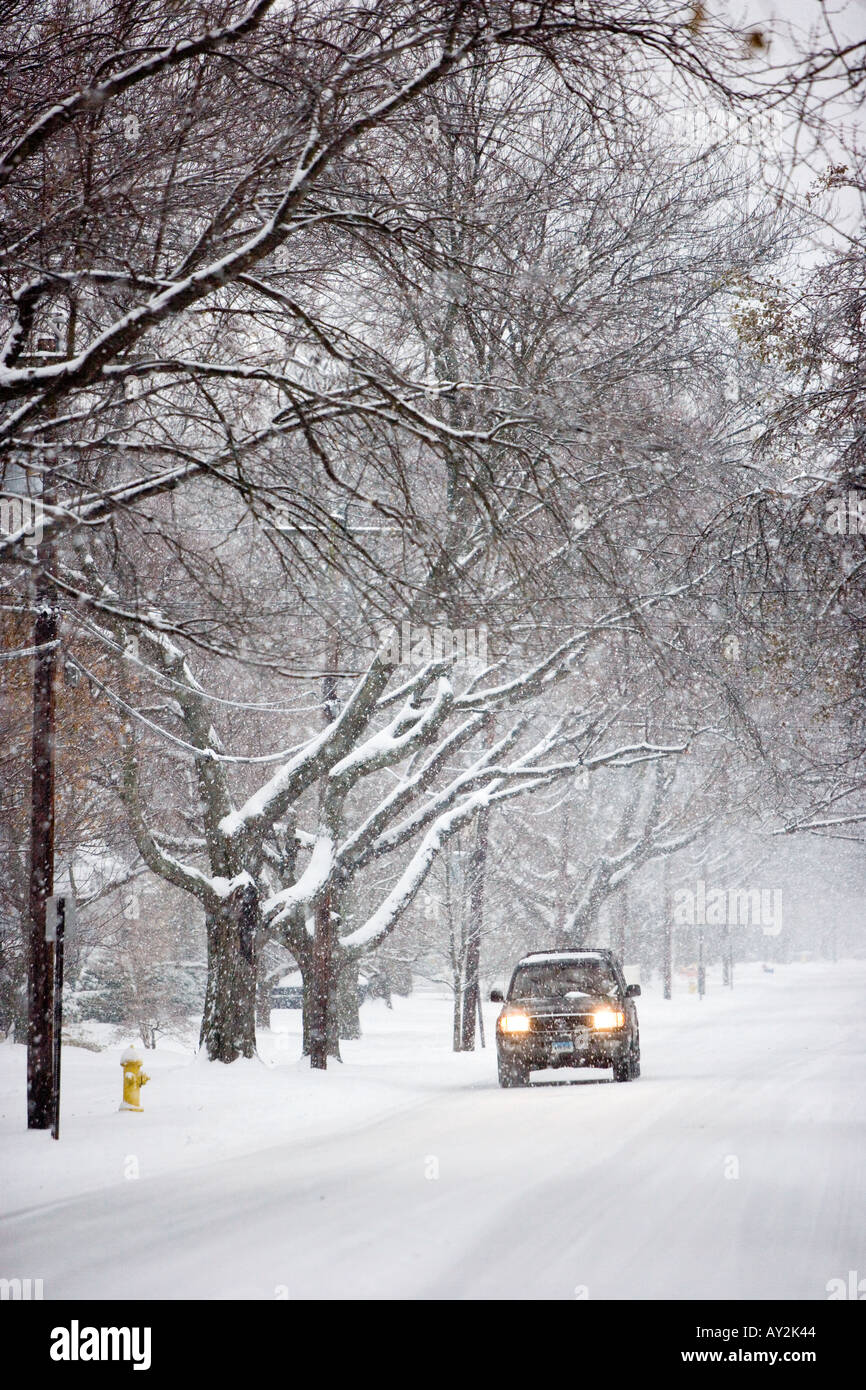 SUV driving down a snowy tree-lined street in a New England town Stock ...