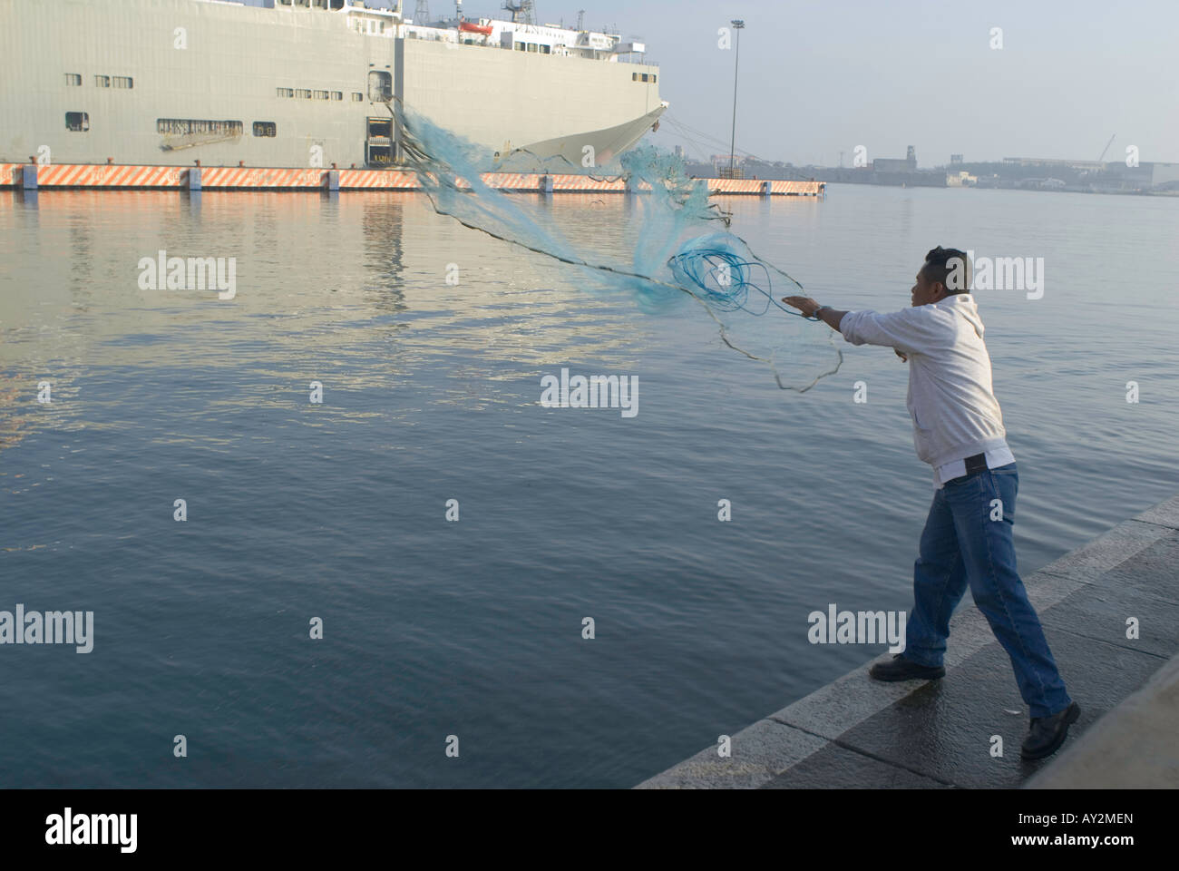 A man casts a fishing net from the docks in the harbor of Veracruz ...