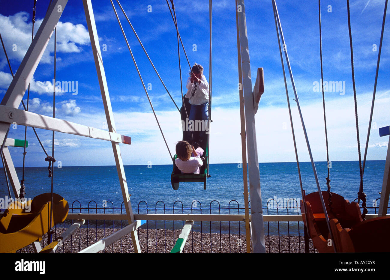 Young children playing on a funfair swing at the seaside in the UK ...