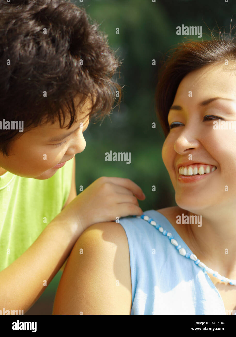 Close-up of a boy putting a necklace around his mother's neck and ...