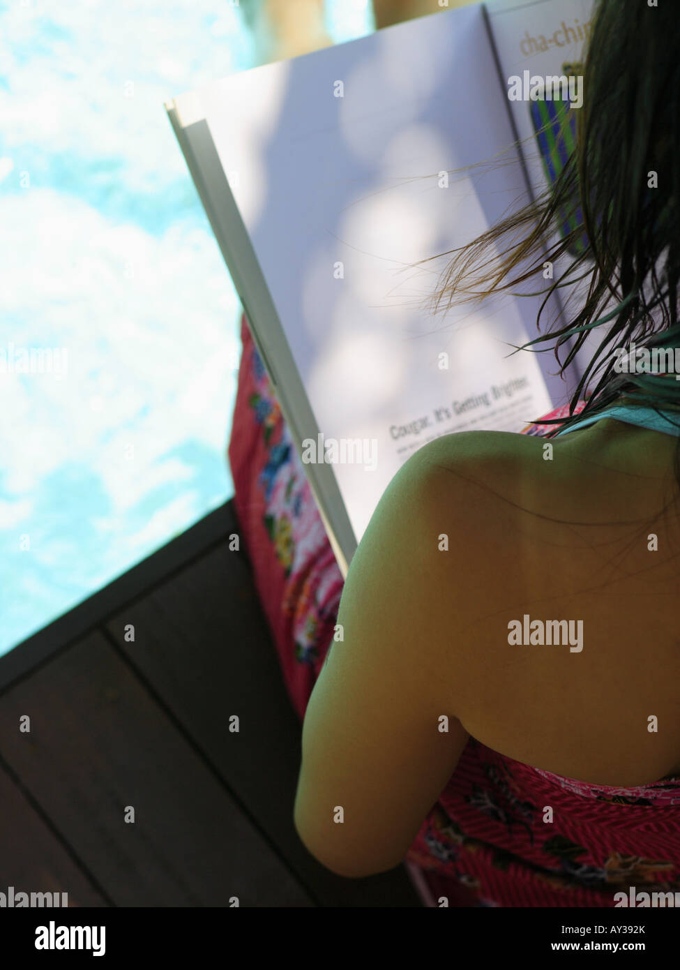 Rear view of a woman reading a book at the poolside Stock Photo - Alamy