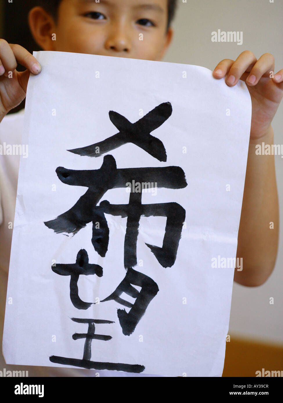 Close-up of a boy showing a Japanese script written on a sheet of paper ...