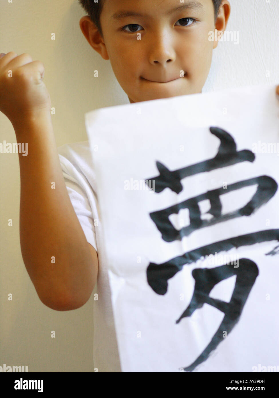 Close-up of a boy showing a Japanese script written on a sheet of paper ...