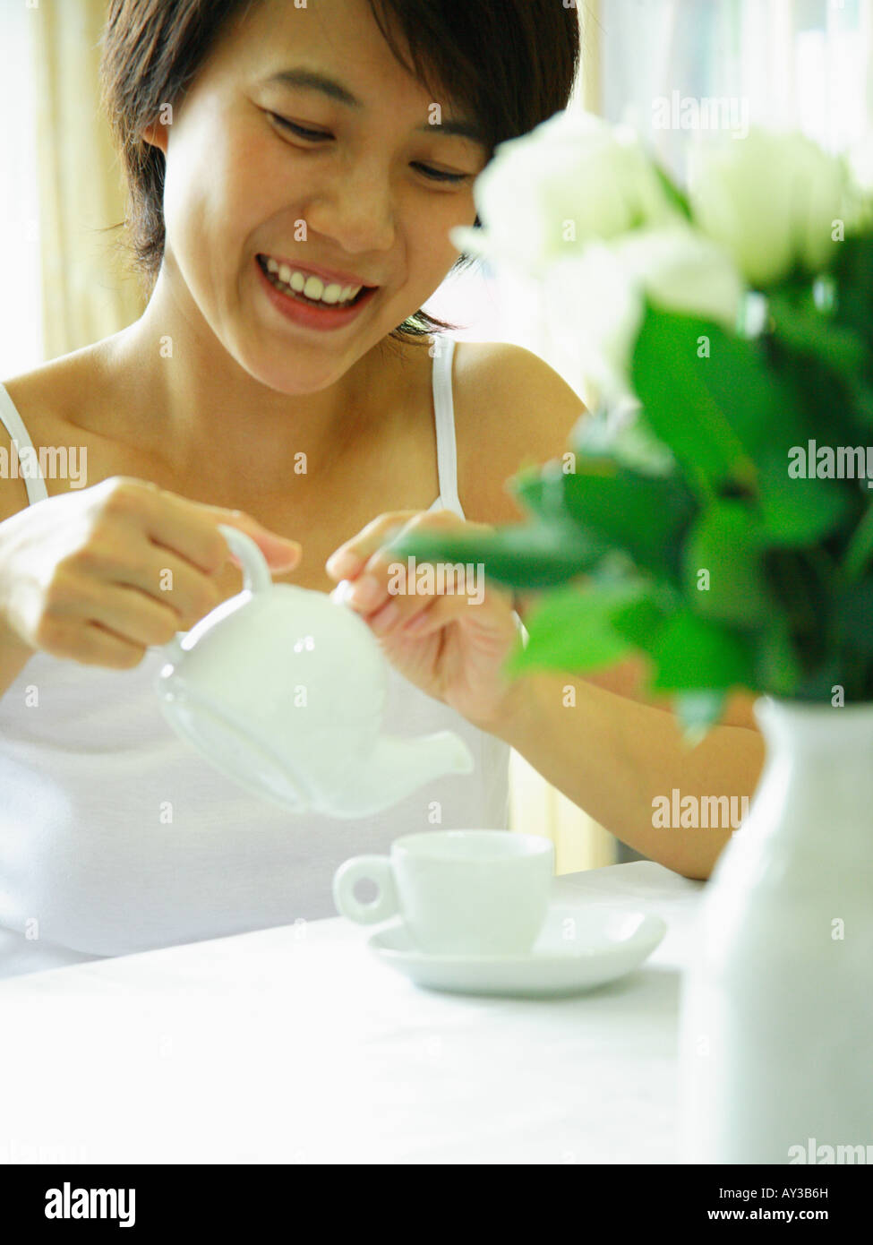 Young woman pouring tea into a cup and smiling Stock Photo - Alamy